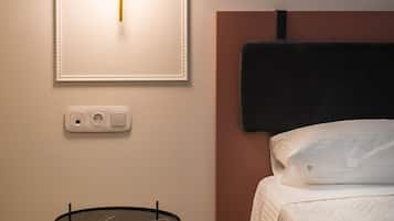 Quarto com cama, mesa de cabeceira, luminária na parede e tomadas.