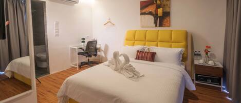 Quarto de hotel com cama, escrivaninha, cadeira, ar condicionado, quadro e mesa de cabeceira com um vaso.