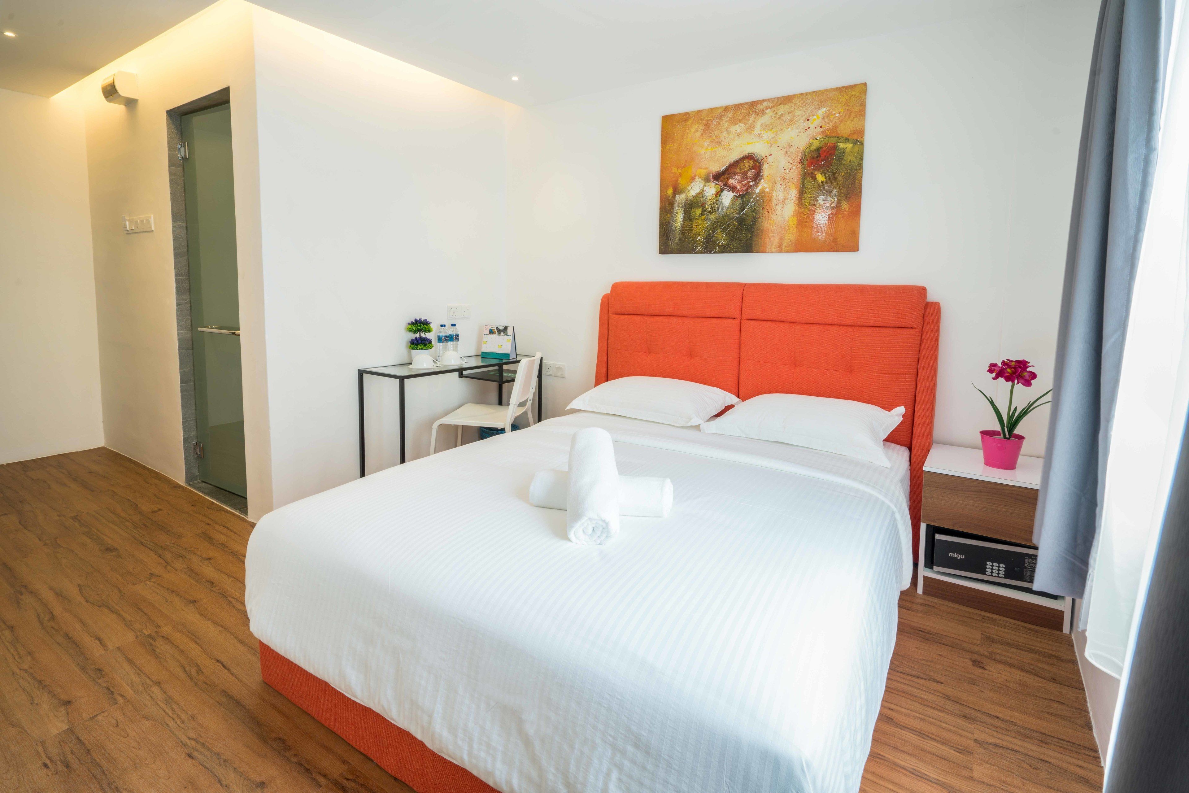 Quarto de hotel com uma cama grande, uma mesa de cabeceira com uma planta, um quadro na parede e uma porta para o banheiro.