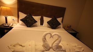 Quarto de hotel com cama bem arrumada, duas almofadas, abajur, telefone e bandeja com lanches.