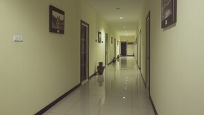 Um corredor longo e bem iluminado, com portas, quadros nas paredes e piso de azulejos.