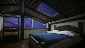 Quarto com vista para um céu estrelado através de claraboias, uma cama de madeira e um tapete estampado.