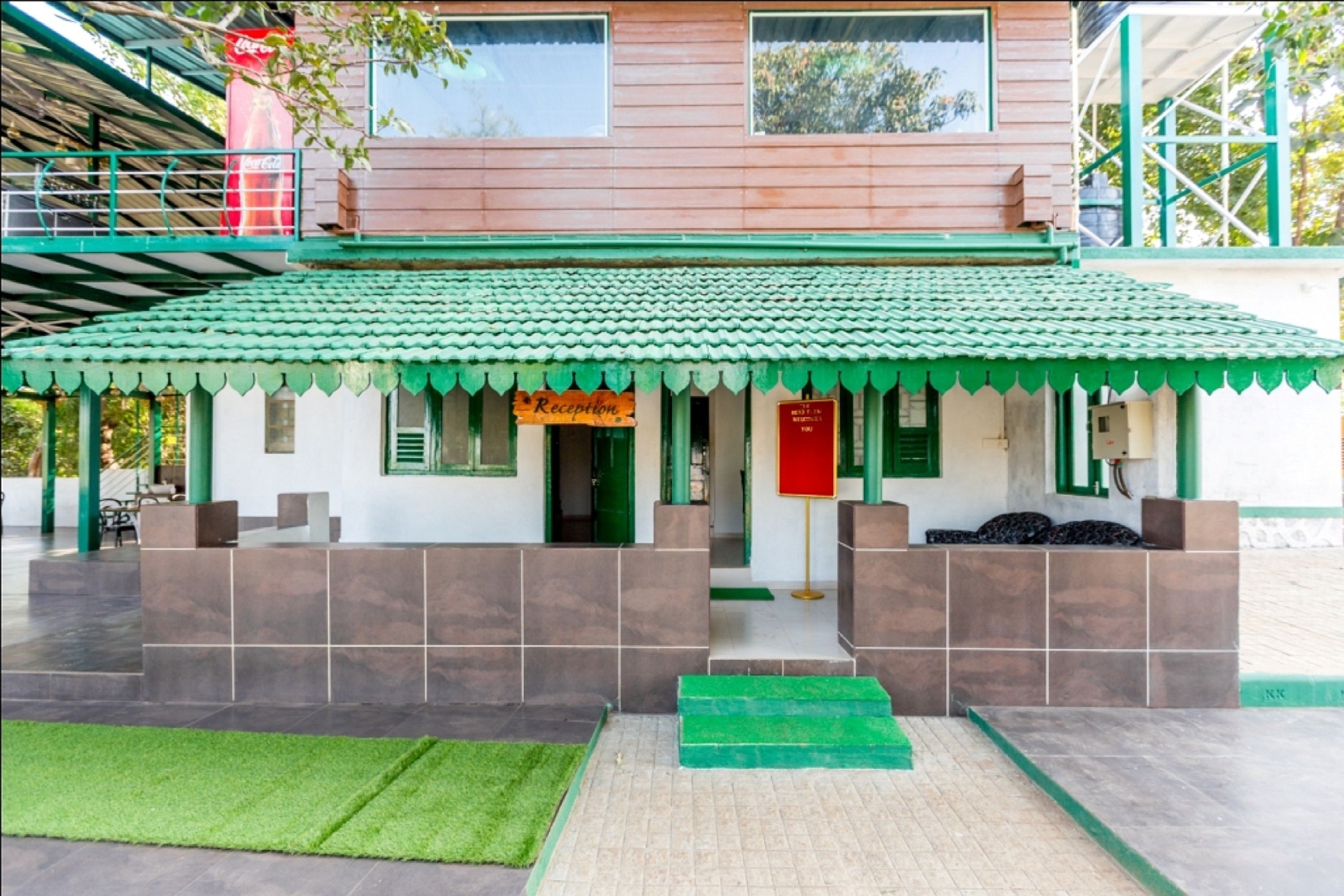 Um edifício com telhado de azulejos verdes, área de recepção e um letreiro da Coca-Cola.
