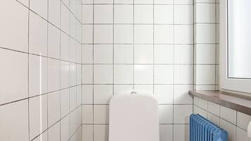 Um banheiro pequeno, com azulejos, um vaso sanitário branco, uma lixeira e um radiador azul.
