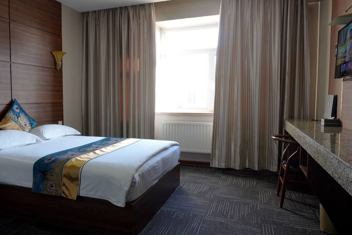 Quarto de hotel com cama, escrivaninha e janela com cortinas.