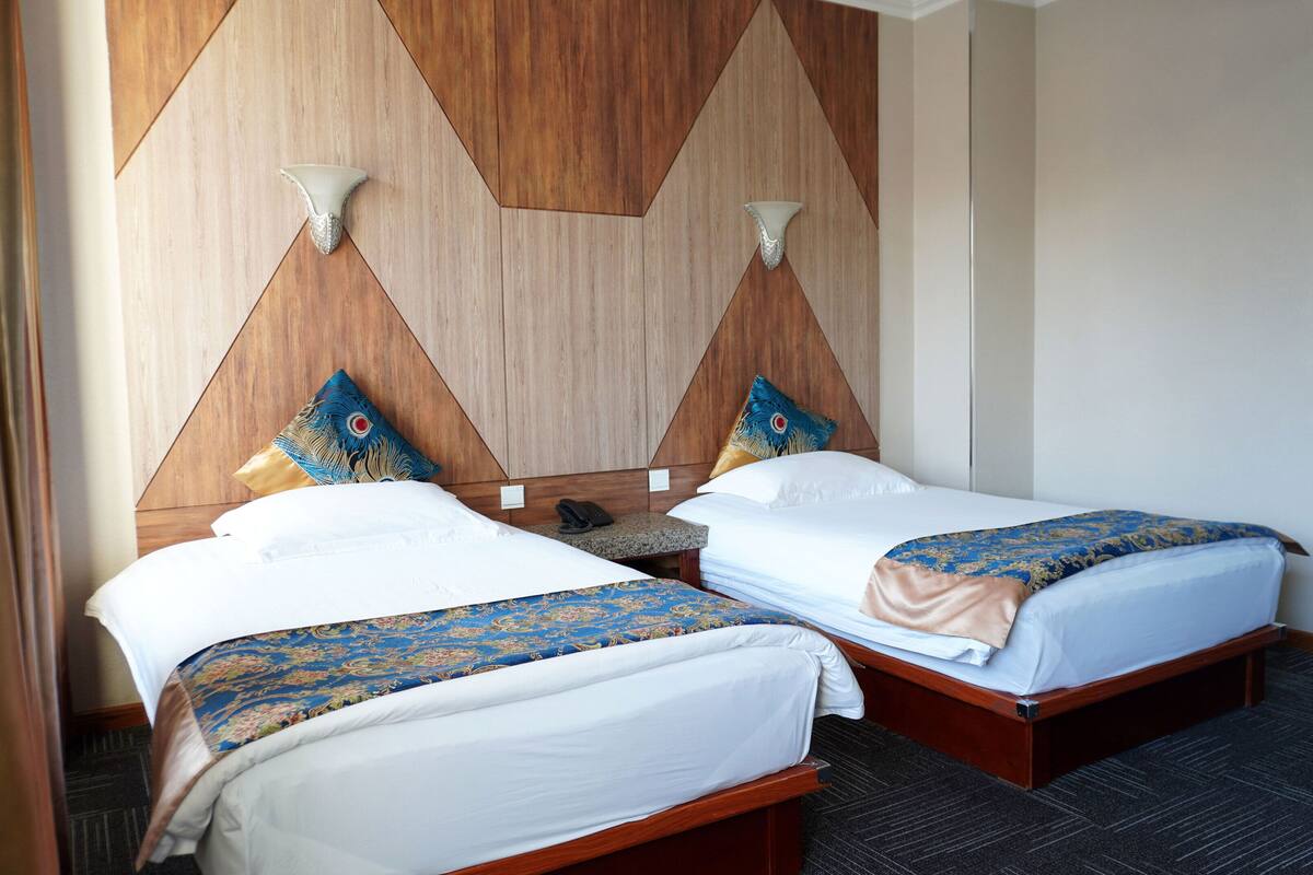 Quarto de hotel com duas camas, cabeceira de madeira e chão coberto por carpete.