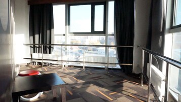 Quarto de hotel com uma grande janela, varanda, mesa e uma cadeira vermelha.