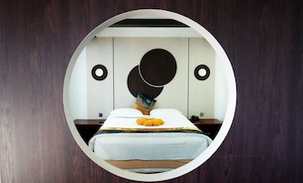 Espelho circular refletindo um quarto com cama, almofadas e mesa de cabeceira.