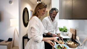Uma cozinha moderna com área de refeições, incluindo uma mesa de madeira, uma cesta de pão e um copo de água.