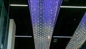 Um interior moderno com escadaria de vidro, parede verde e teto decorado com luzes verticais.