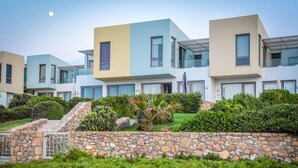 Edifício residencial moderno com muro de pedra, vegetação exuberante e céu claro.