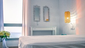 Quarto com cama, mesa de cabeceira, espelho, luminária na parede e janela com cortinas.