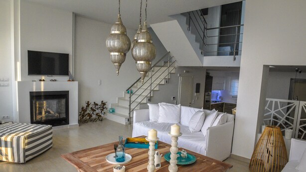 Uma sala de estar moderna com lareira, um sofá branco, uma mesa de centro de madeira e luminárias pendentes.