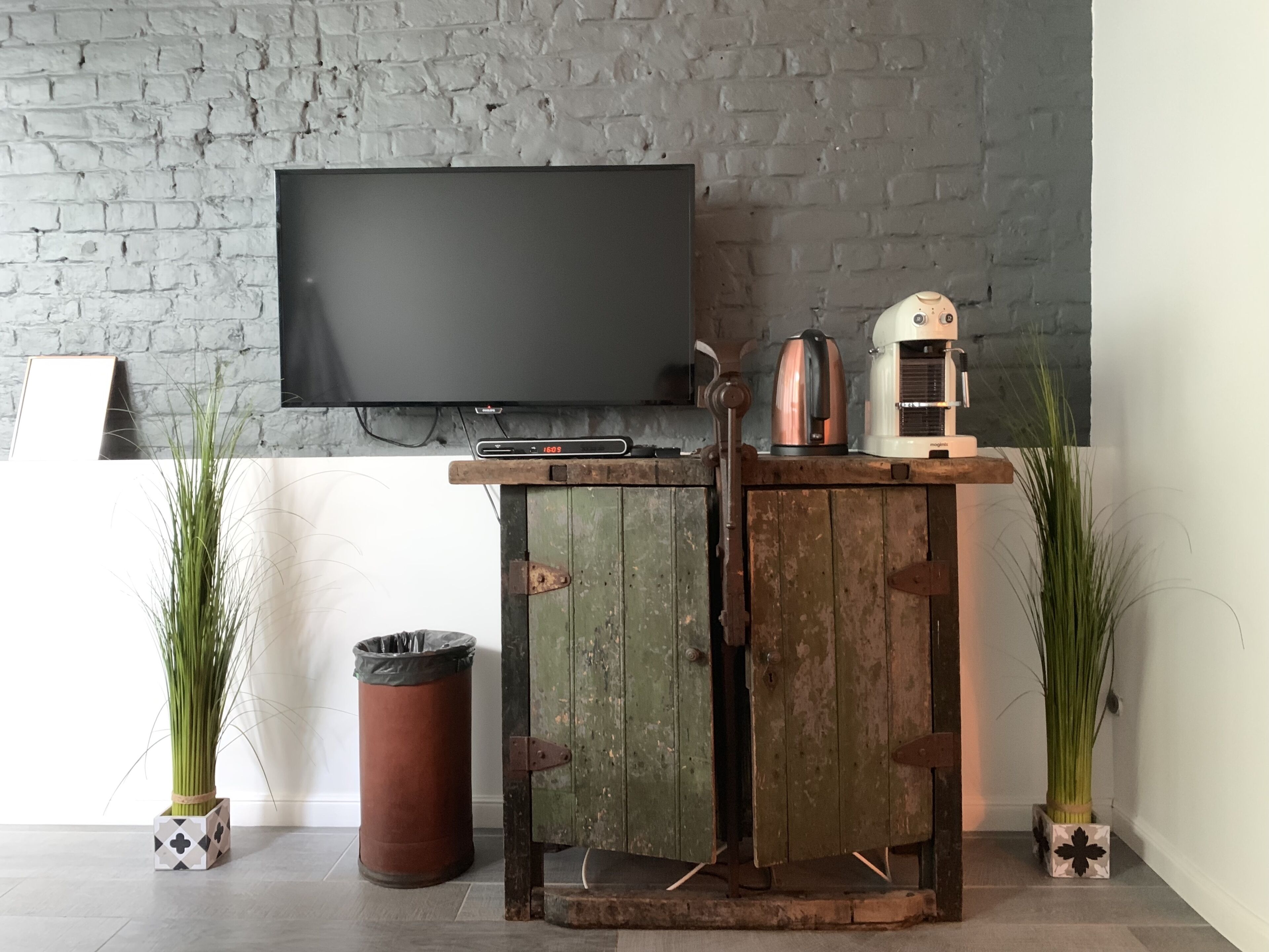 Um armário de madeira rústico com uma televisão montada acima, uma cafeteira antiga e duas plantas em vasos.