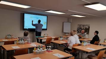 Uma sala de aula com tela de projeção, mesas com garrafas e um projetor.