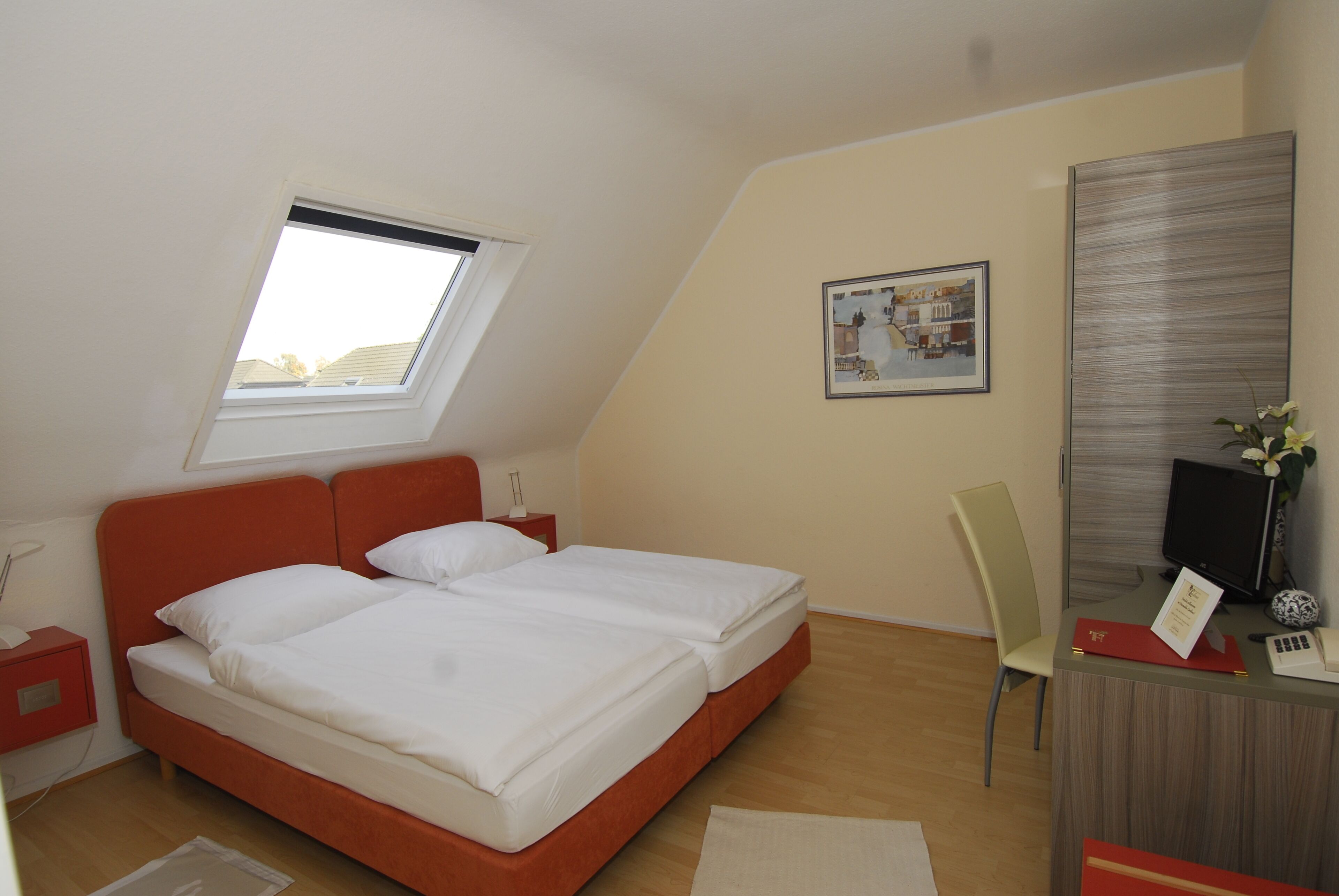 Quarto com cama, escrivaninha, cadeira, janela e um quadro na parede.