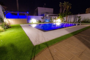 Piscina com deck ladrilhado, rodeada por um gramado bem cuidado e cerca de madeira.