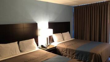 Quarto de hotel com duas camas, uma mesa de cabeceira, uma luminária e uma janela com cortinas.