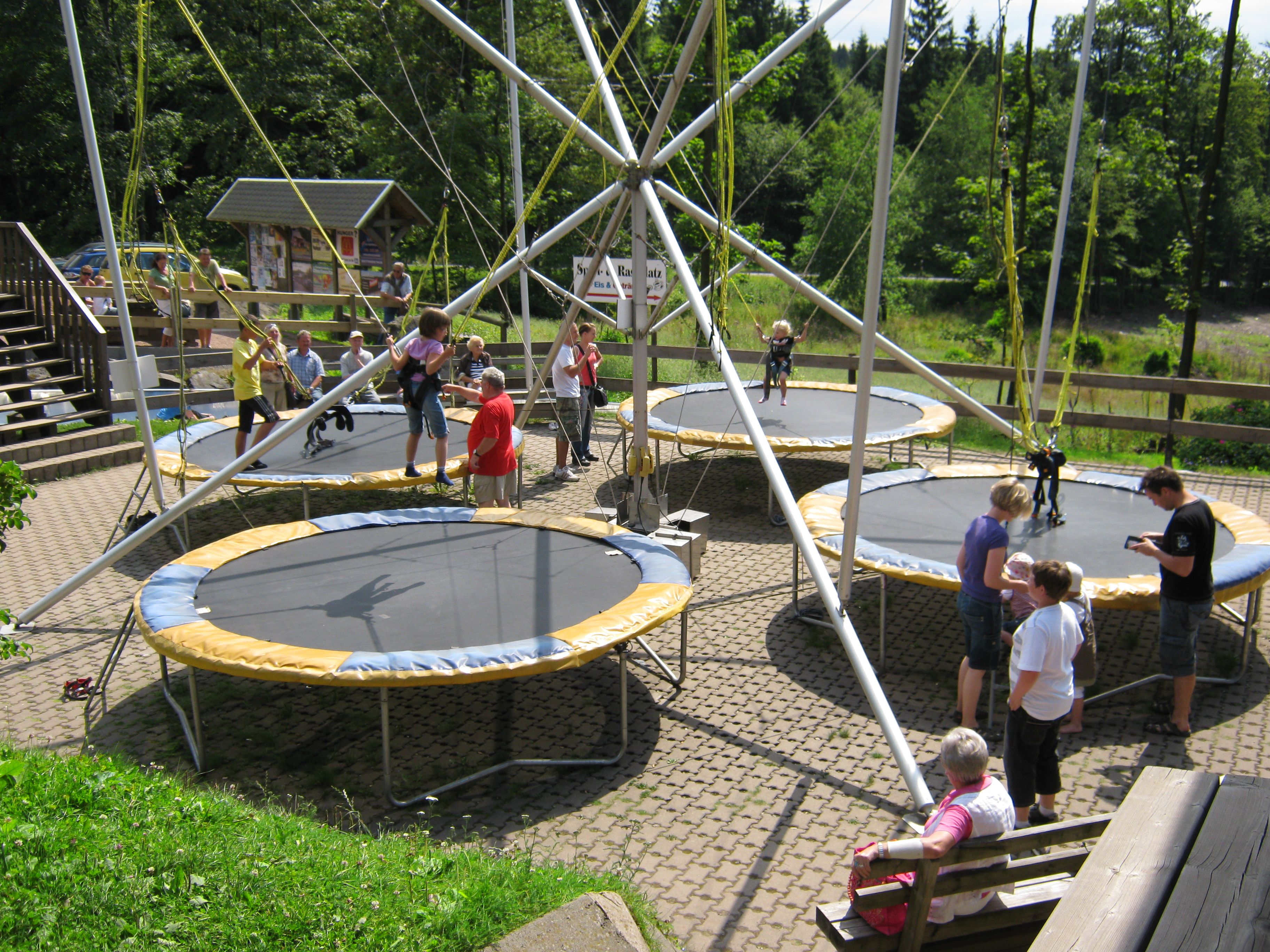 Um parquinho com vários trampolins e uma estrutura de madeira ao fundo.