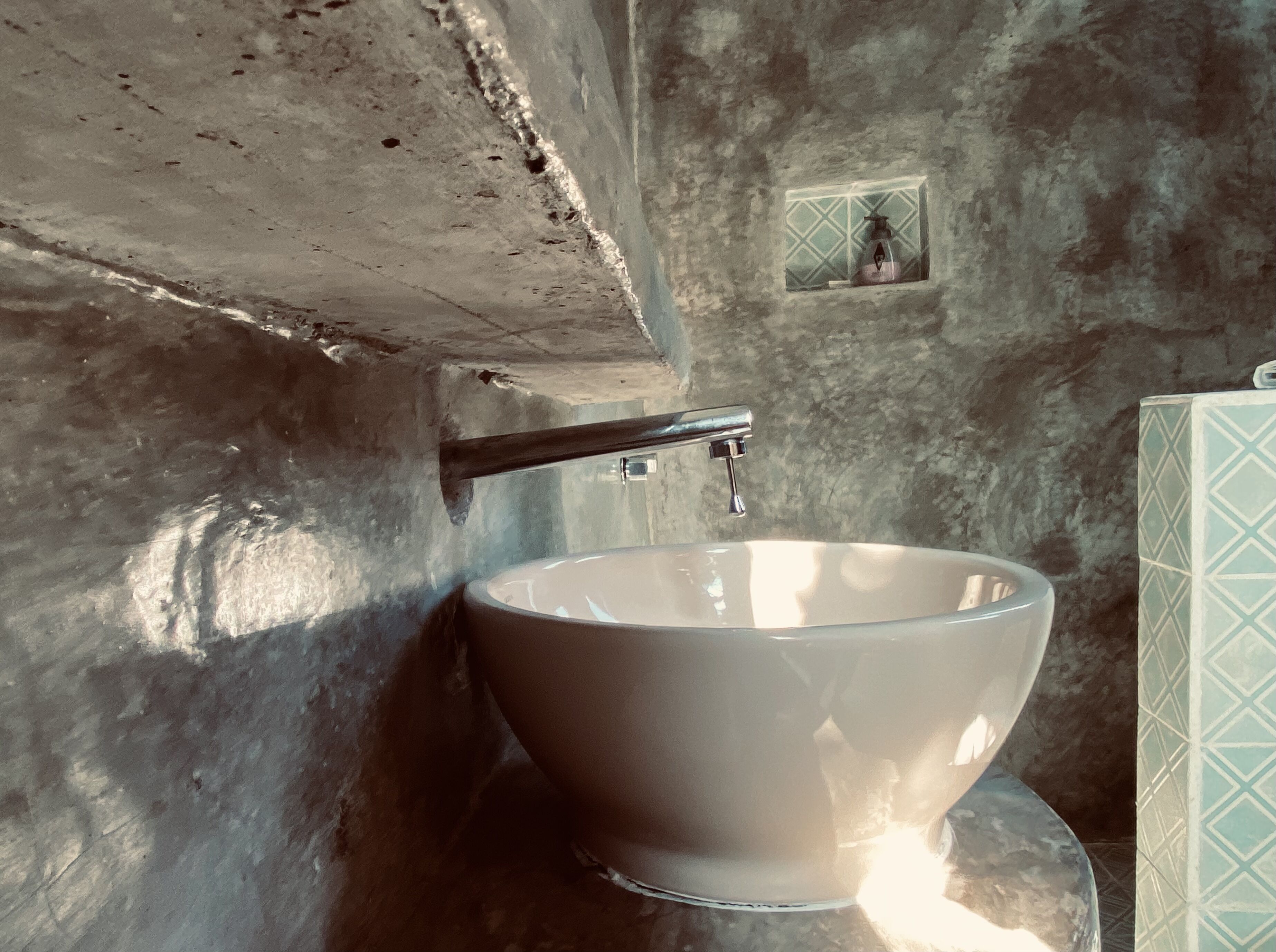 Casa de banho com uma pia branca, uma pequena janela e uma parede revestida a azulejos.
