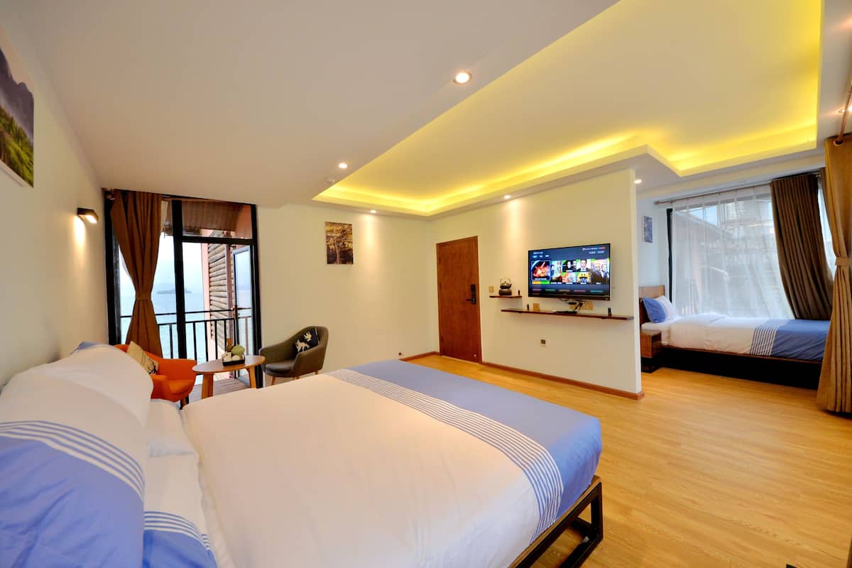 Quarto de hotel com uma cama grande, uma cama menor, uma televisão, uma escrivaninha e uma cadeira.