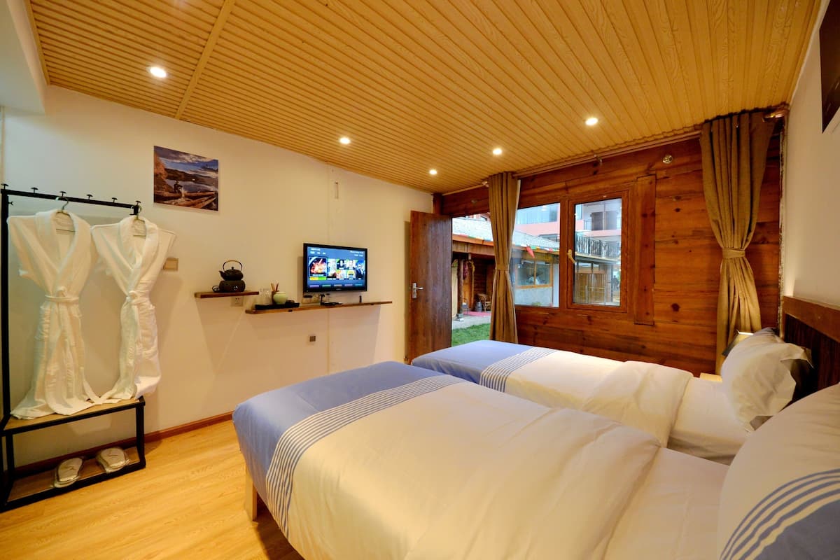 Quarto de hotel com duas camas, televisão, teto de madeira e janela com cortinas.