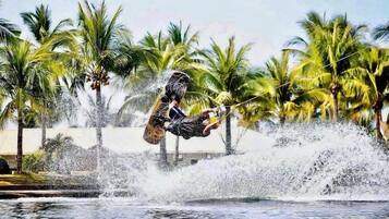 Um atleta de wakeboard em pleno voo sobre a água, cercado por palmeiras.