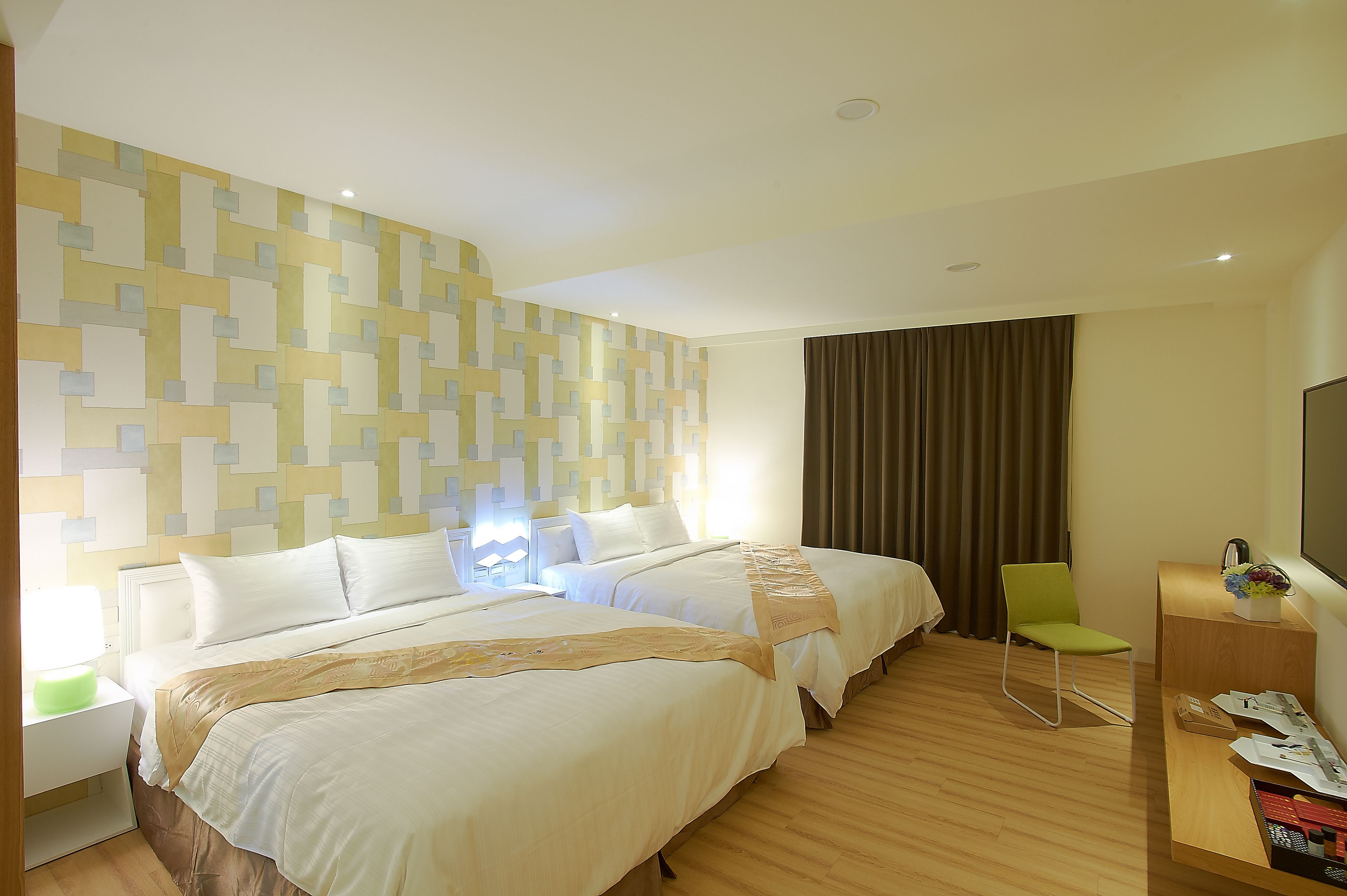 Quarto de hotel com duas camas, piso de madeira, escrivaninha com cadeira e televisão.