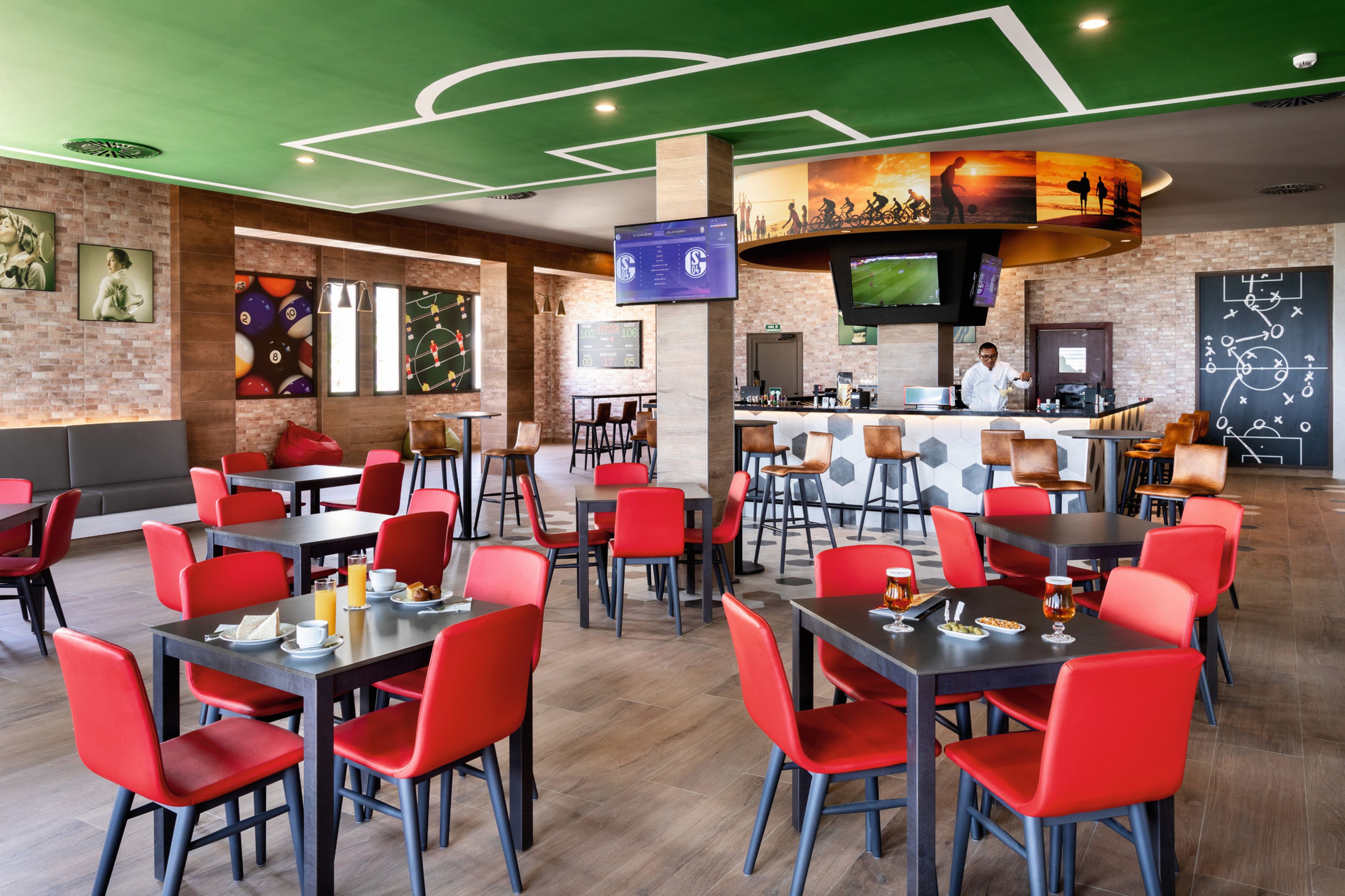 Um restaurante moderno com cadeiras e mesas vermelhas, um espaço de bar e decoração temática esportiva.