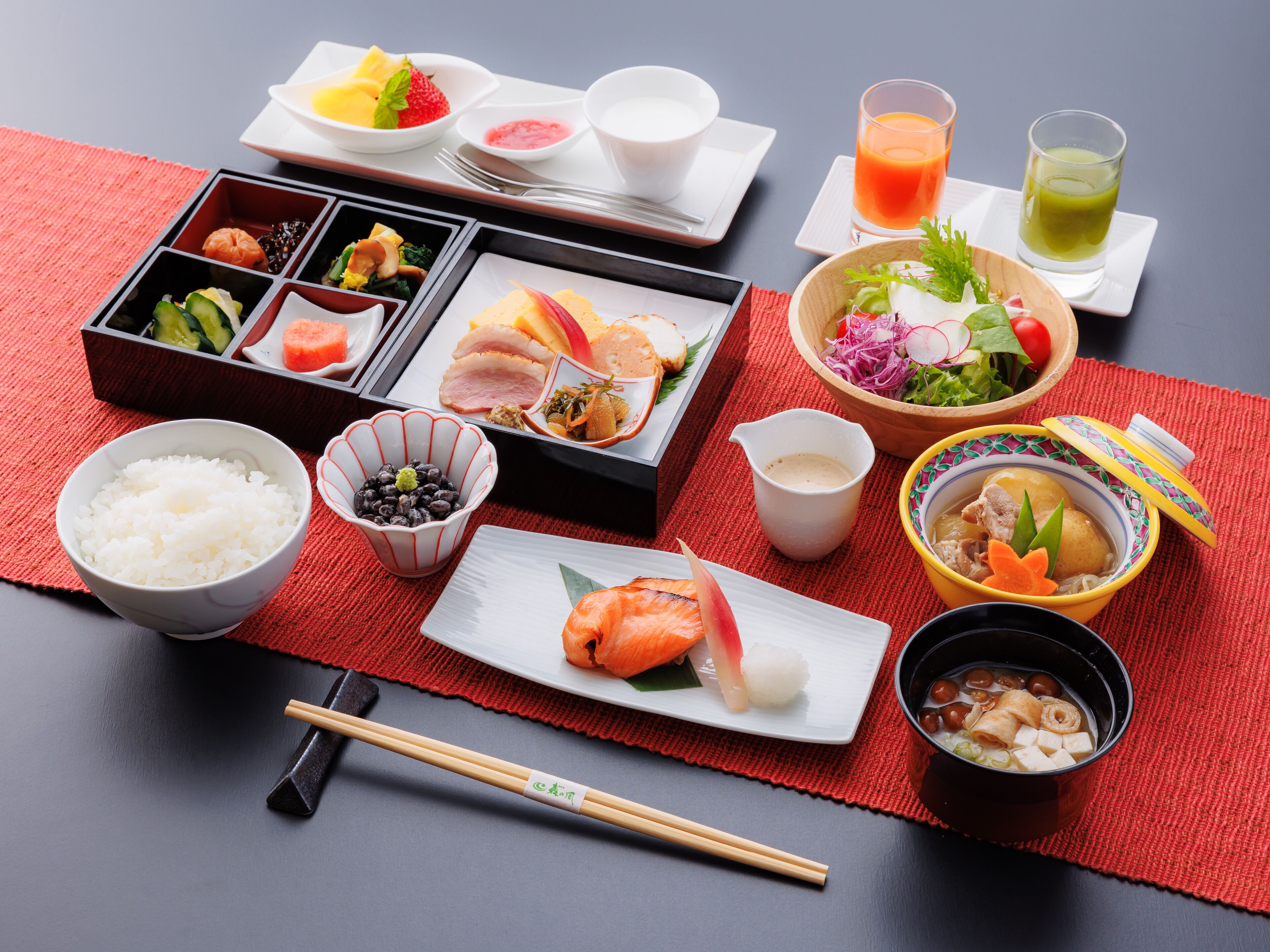 Diversos pratos japoneses, incluindo sushi, arroz e sopa, dispostos sobre uma mesa com hashis e um jogo de toalha de mesa vermelho.
