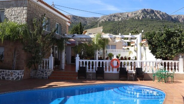 Piscina com cerca branca e cadeiras, cercada por edifícios com paredes de pedra e um cenário montanhoso.