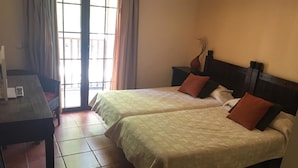 Quarto com duas camas, uma mesa e janela com cortinas.