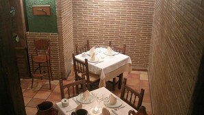 Uma área de refeições com parede de tijolos, uma mesa posta para quatro com toalhas brancas e cerâmica rústica sobre a mesa.