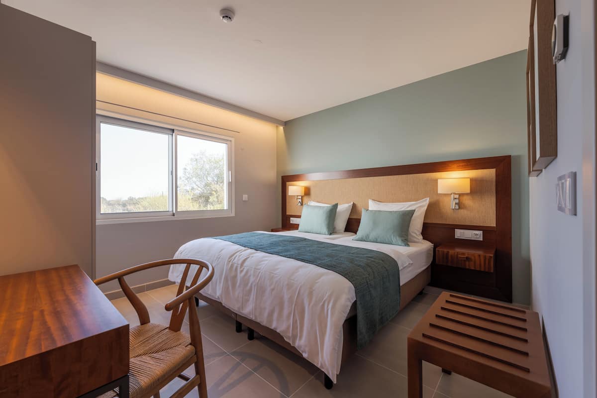 Quarto de hotel com uma cama grande, mesas de cabeceira, escrivaninha e uma cadeira.