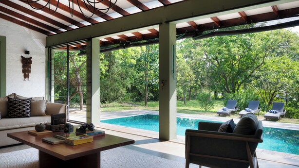 Uma sala de estar moderna com vista para a piscina, um sofá, uma mesa de centro e uma poltrona.