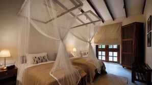 Quarto com duas camas, cada uma com dossel, mesa de cabeceira com abajur e guarda-roupa de madeira.