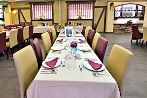 Uma mesa de jantar comprida disposta com várias cadeiras, cada uma com toalha de mesa branca e guardanapos roxos.
