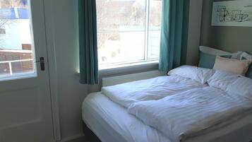 Quarto com cama, janela com cortinas, radiador e porta.