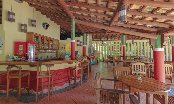 Restaurante com mobiliário de madeira, um bar e chão ladrilhado.