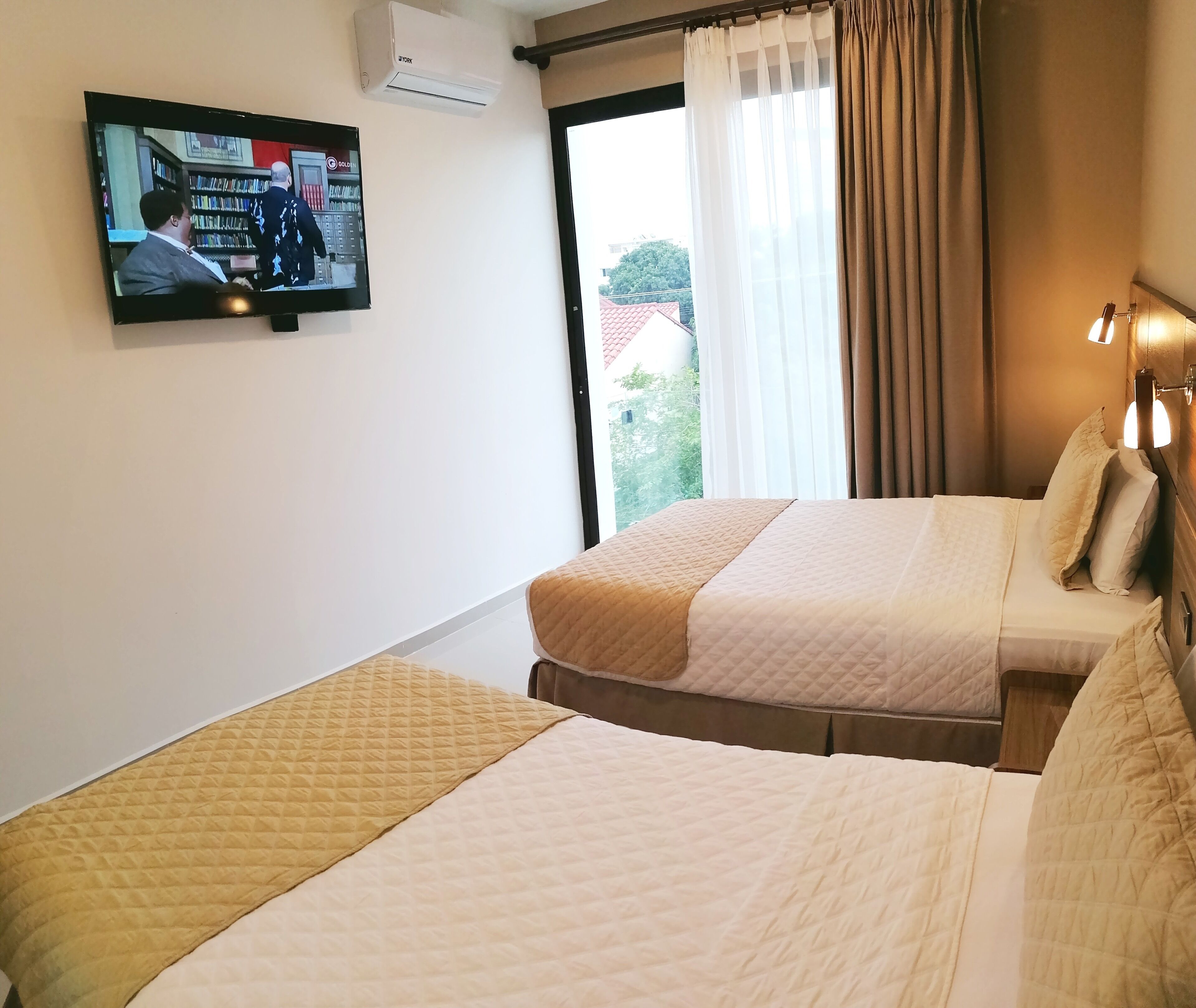 Quarto de hotel com duas camas, uma televisão na parede e uma janela com cortinas.