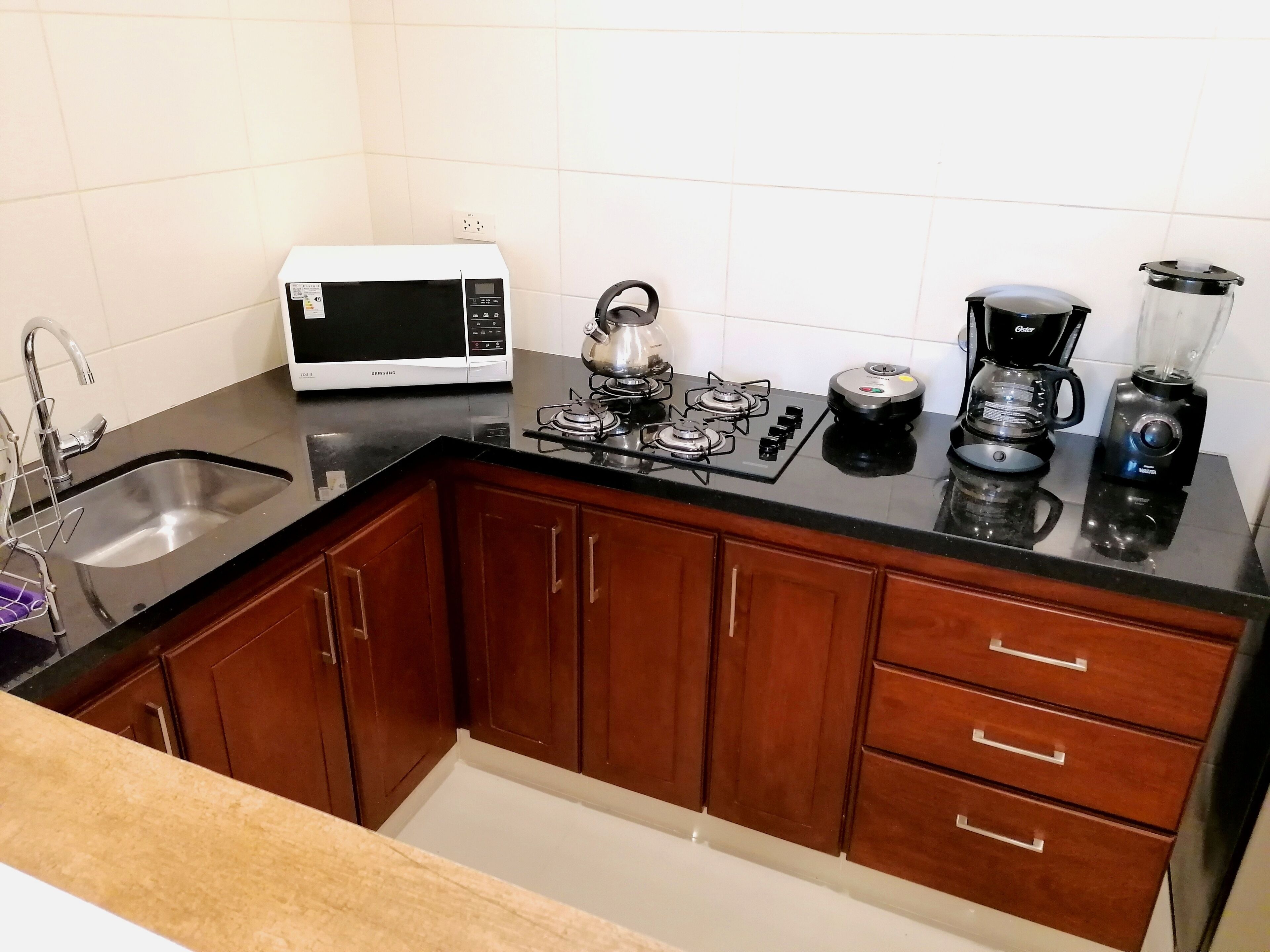 Uma cozinha equipada com micro-ondas, chaleira, máquina de café, liquidificador e pia.