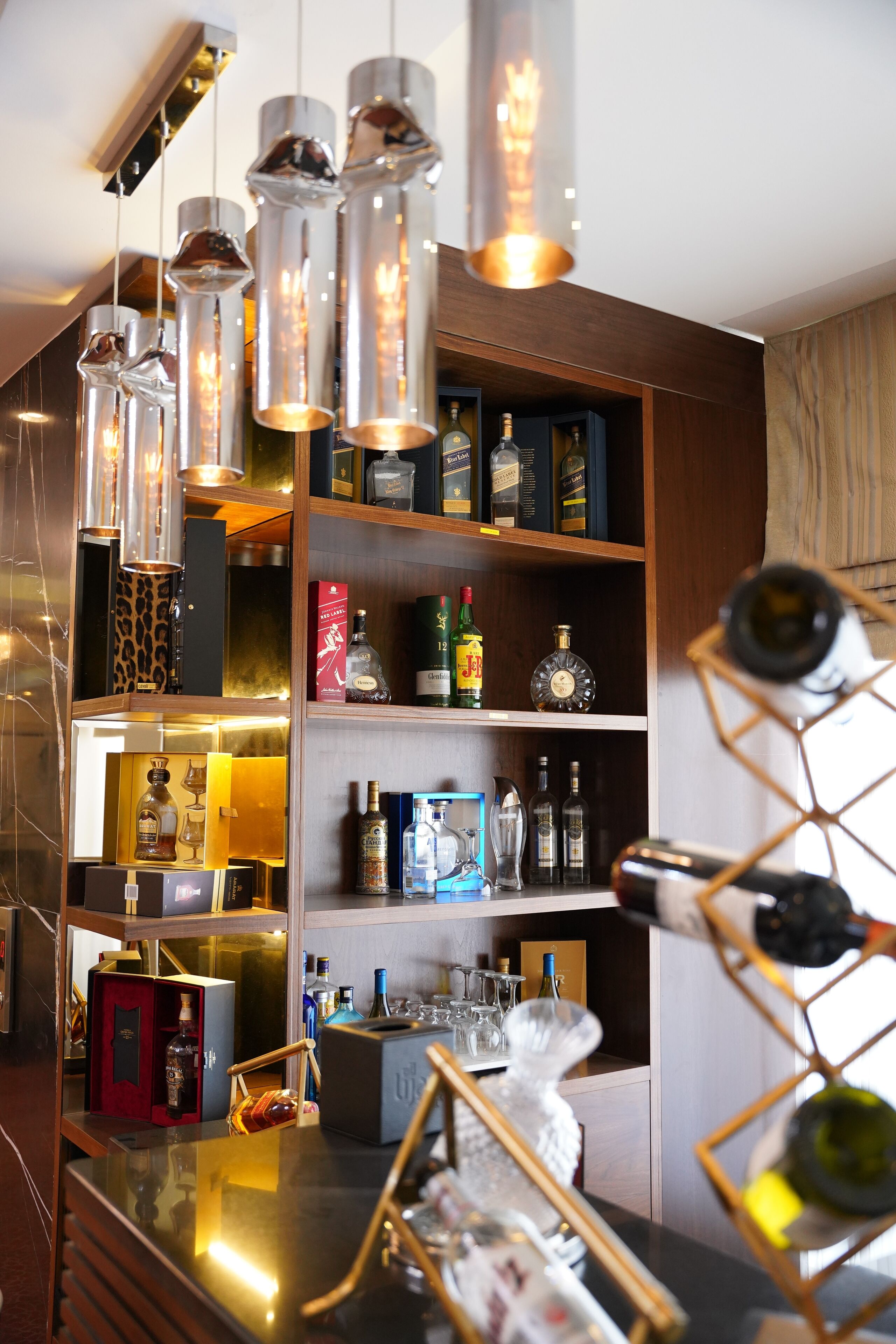 Uma área de bar com prateleiras cheias de garrafas de bebidas, um esguicho para vinhos e luminárias pendentes.