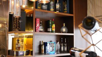 Uma área de bar com prateleiras cheias de garrafas de bebidas, um esguicho para vinhos e luminárias pendentes.