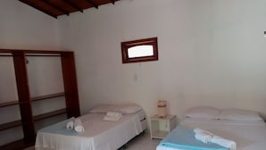 Quarto com duas camas, uma janela pequena e uma prateleira de madeira.