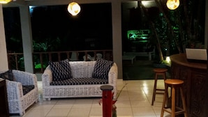 Uma área externa bem iluminada com móveis de vime, uma mesa pequena e luminárias pendentes.