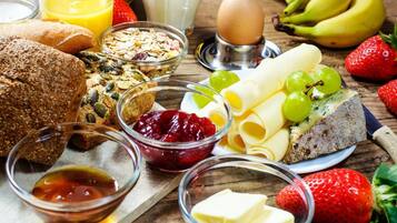 Diversas opções de pequeno-almoço, incluindo pão, cereais, queijo, fruta e acompanhamentos.