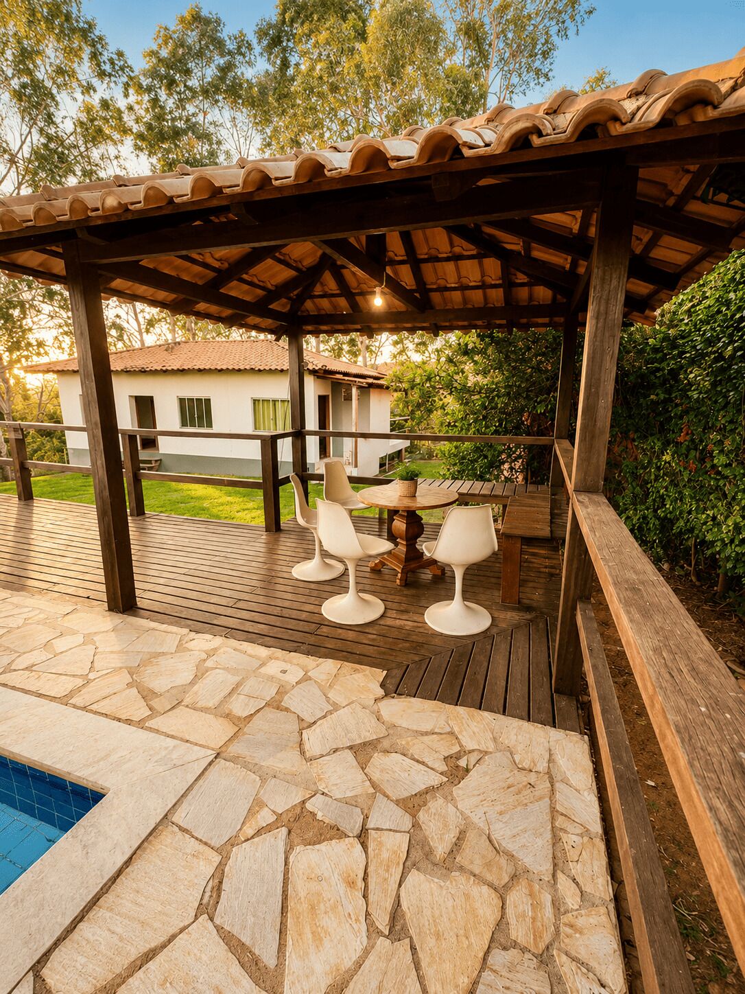 Uma área externa coberta com deck de madeira, piso de pedra e piscina.