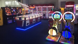 Um salão de jogos bem iluminado com diversas máquinas, incluindo jogos de garra e de corrida.