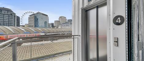 Quarto de hotel com uma grande janela com vista para uma estação de trem e uma roda gigante.