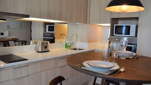 Uma cozinha moderna com uma ilha central, eletrodomésticos de aço inoxidável e uma área de refeições com mesa redonda para quatro pessoas.